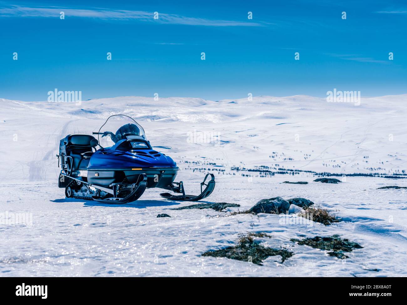 One blue snowmobile stands on a crust snow in Norwegian mountains, warm ...
