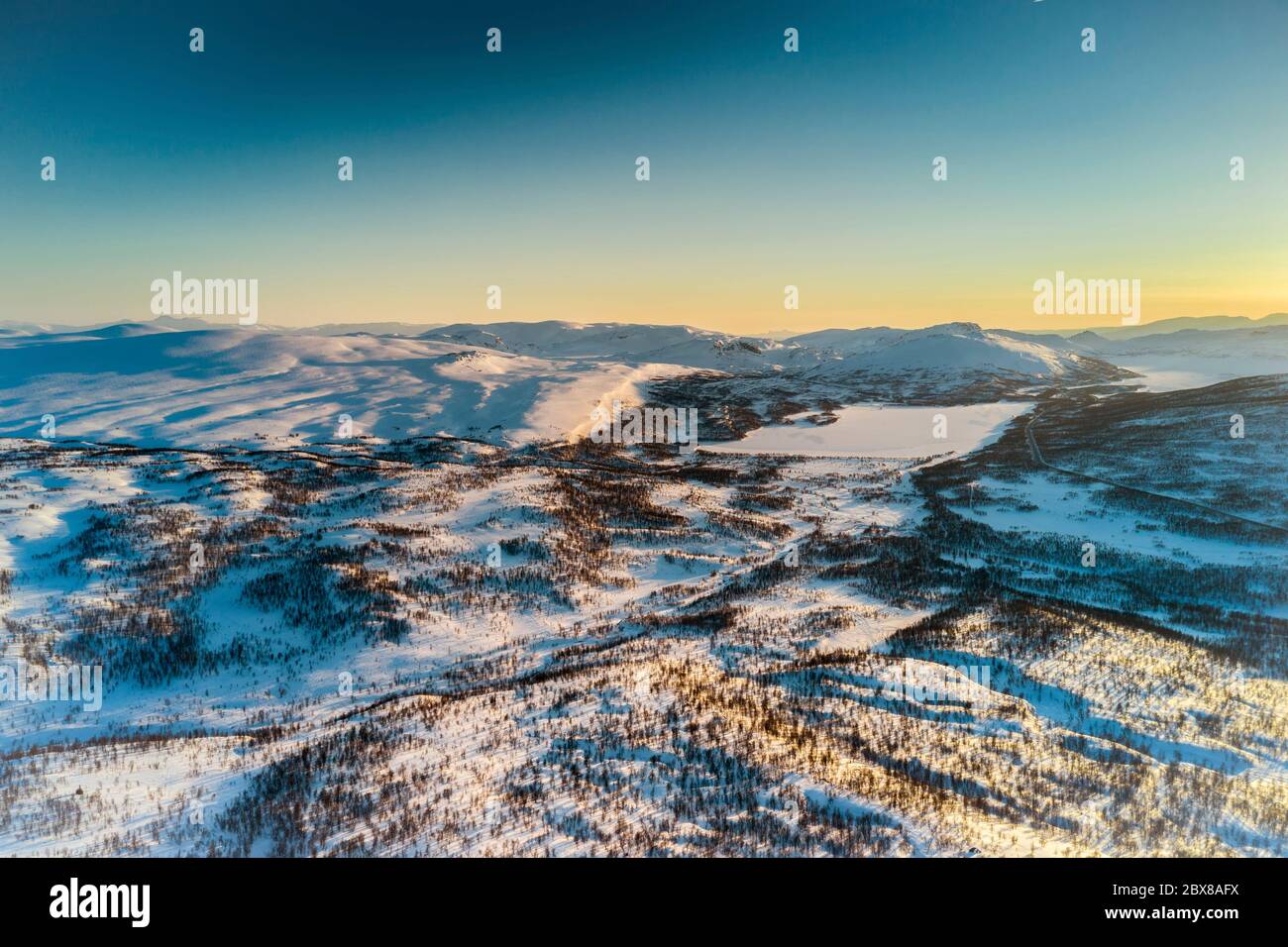 Aerial: Sunset golden light over Norwegian snowy winter mountains with ...