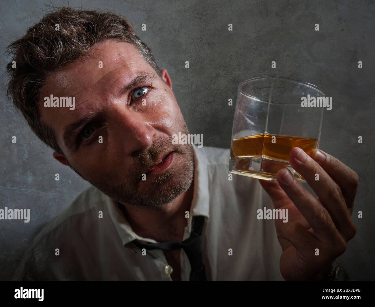 dramatic portrait of 30s to 40s alcoholic man in lose necktie drinking ...