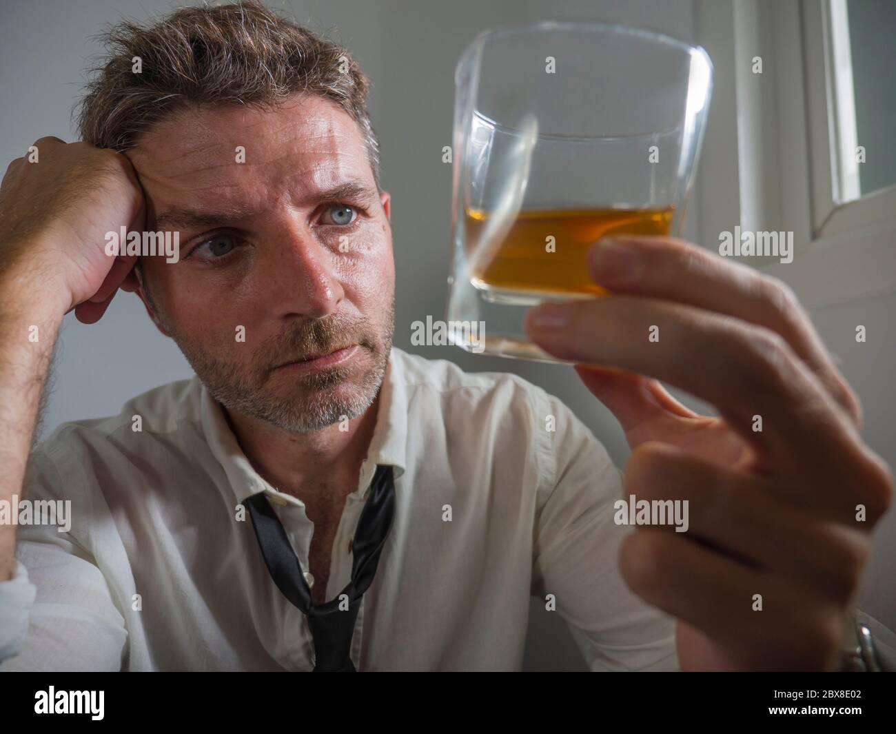 dramatic portrait of 30s to 40s alcoholic man in lose necktie drinking ...