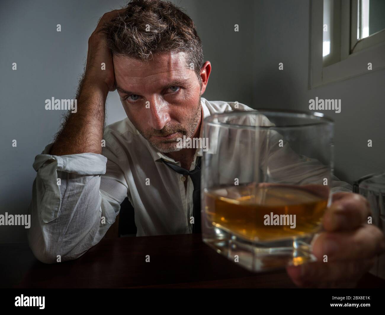 dramatic portrait of 30s to 40s alcoholic man in lose necktie drinking ...