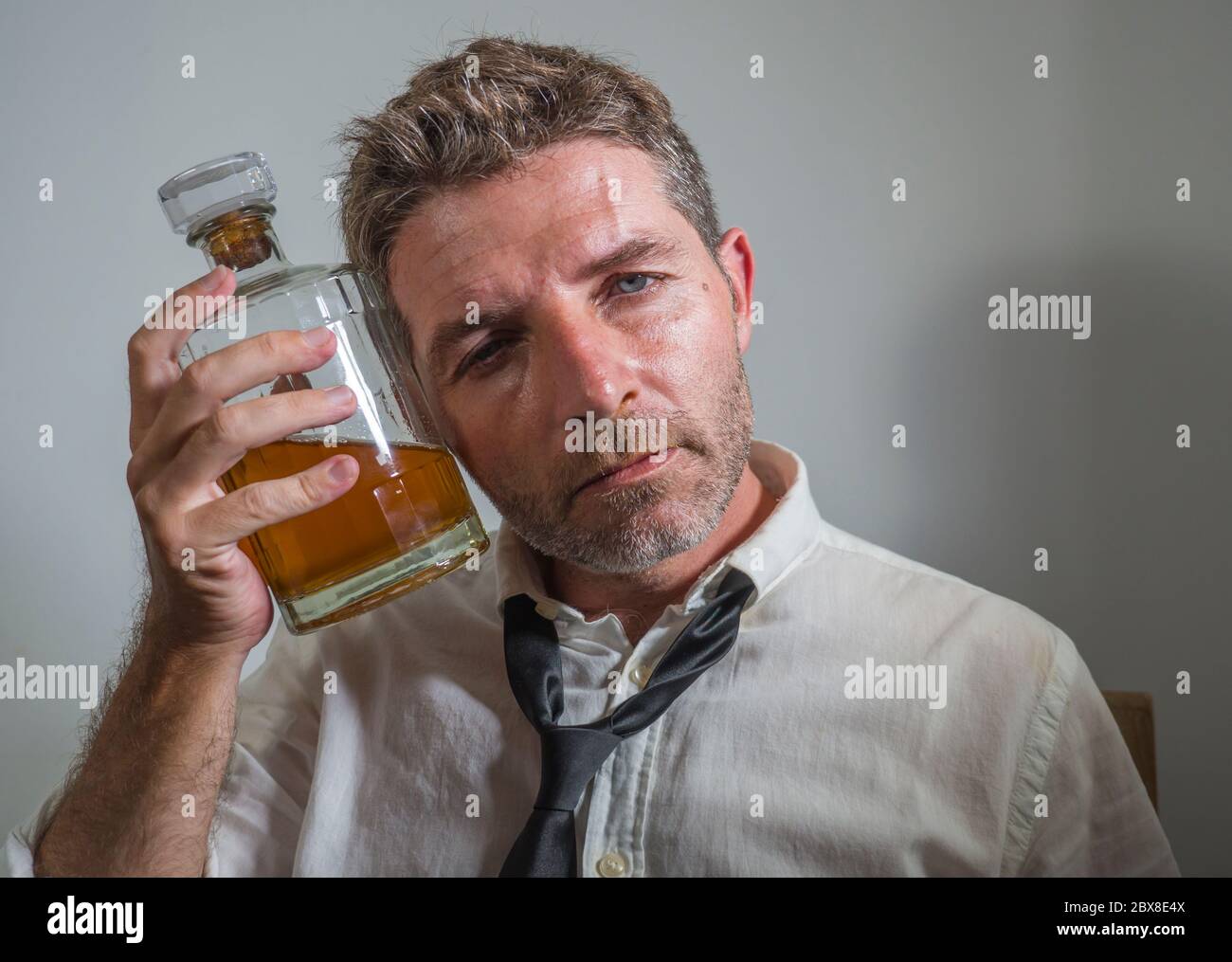 dramatic portrait of 30s to 40s alcoholic man in lose necktie drinking ...