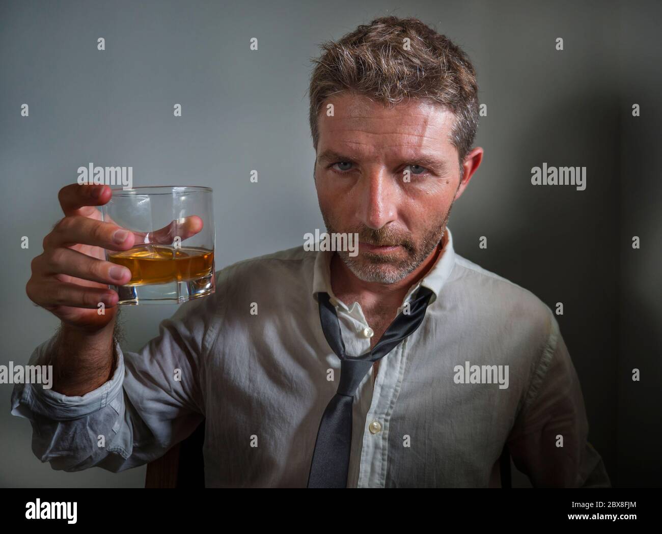 dramatic portrait of 30s to 40s alcoholic man in lose necktie drinking ...