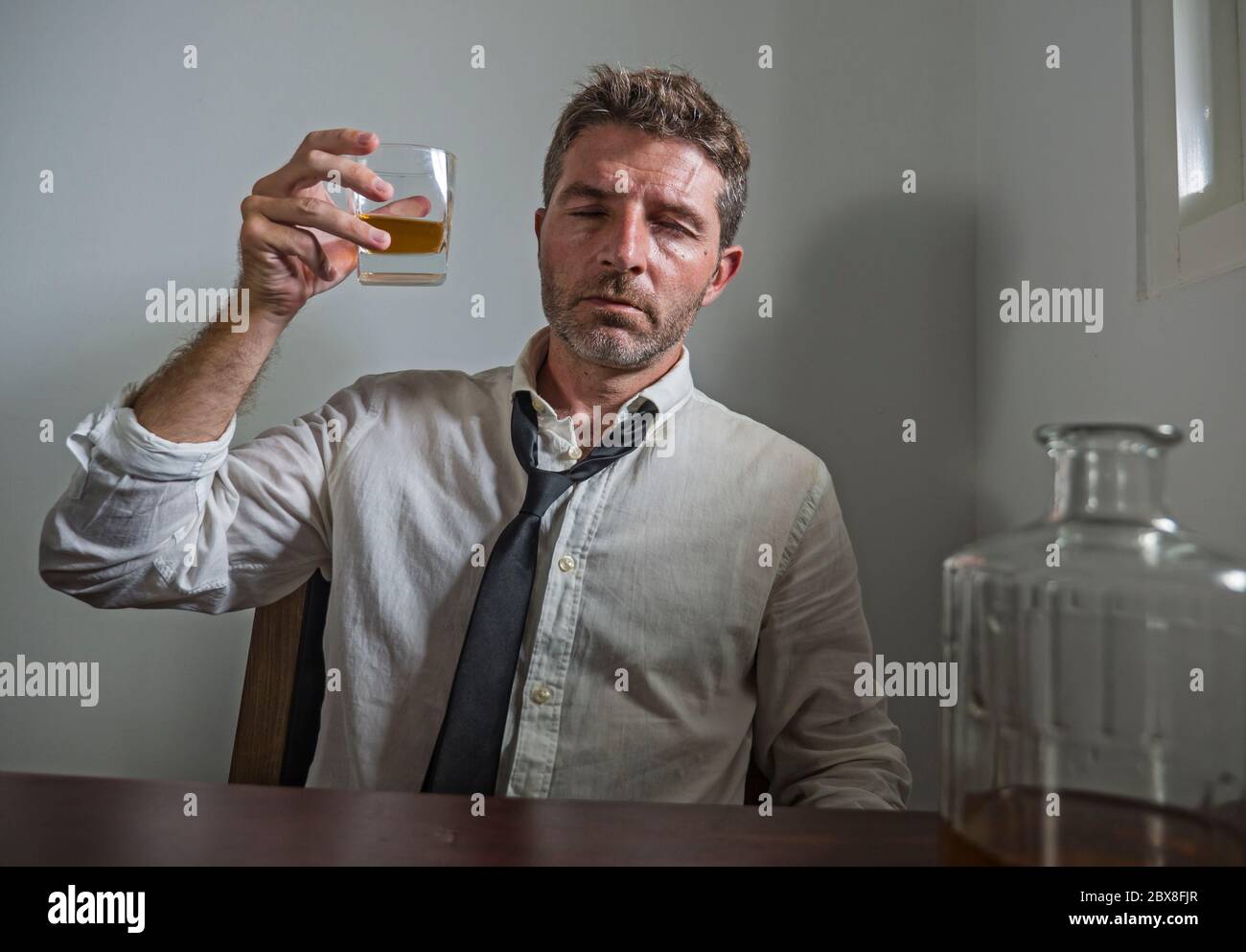 dramatic portrait of 30s to 40s alcoholic man in lose necktie drinking ...