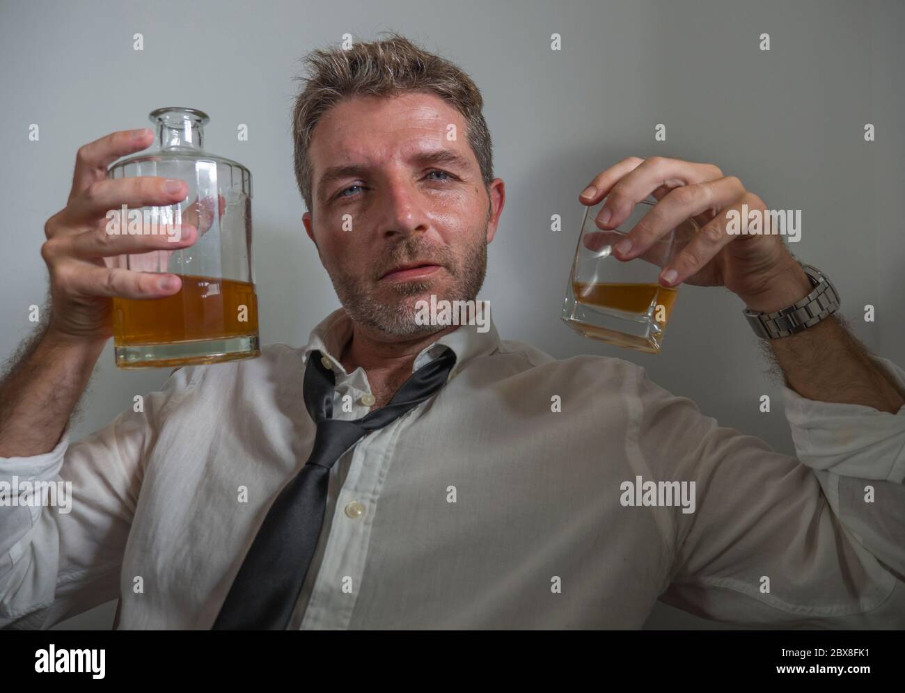 dramatic portrait of 30s to 40s alcoholic man in lose necktie drinking ...