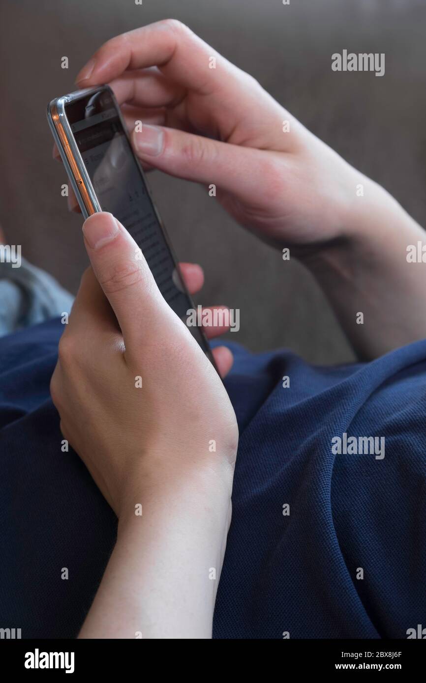 Man lying on the couch and scrolling and reading messages on his smartphone. Narrow depth of ...
