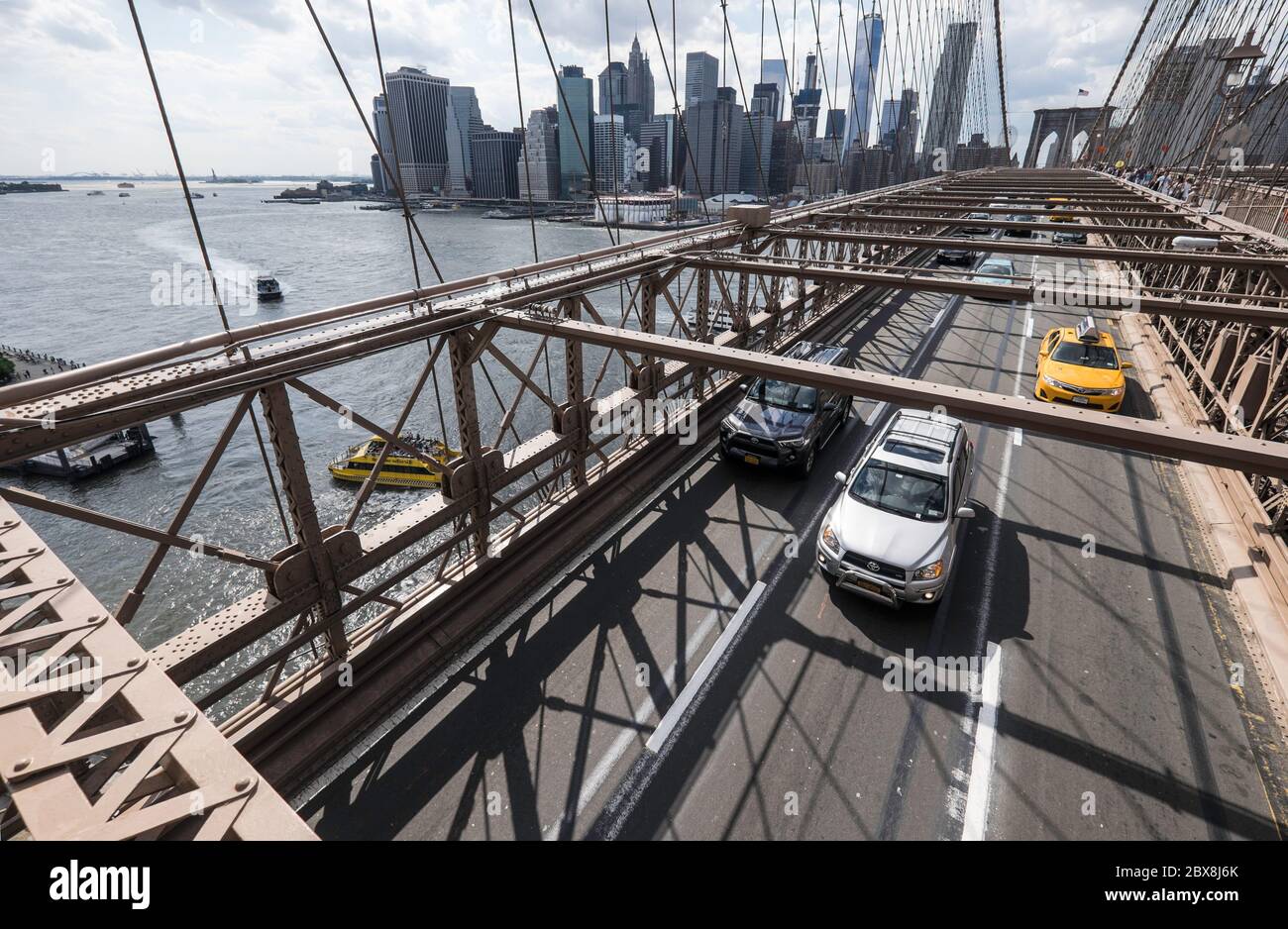 Cars speeding in sun on Brooklyn Bridge with skyline, Manhattan. One of ...