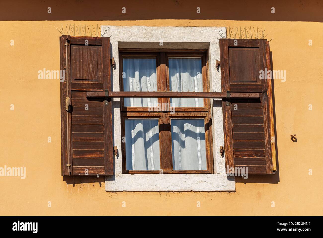 Close-up of a window with open brown wooden shutters with spike steel ...
