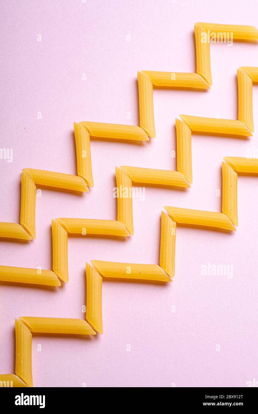 Italian pasta, raw penne tube macaroni zigzag pattern on pink ...