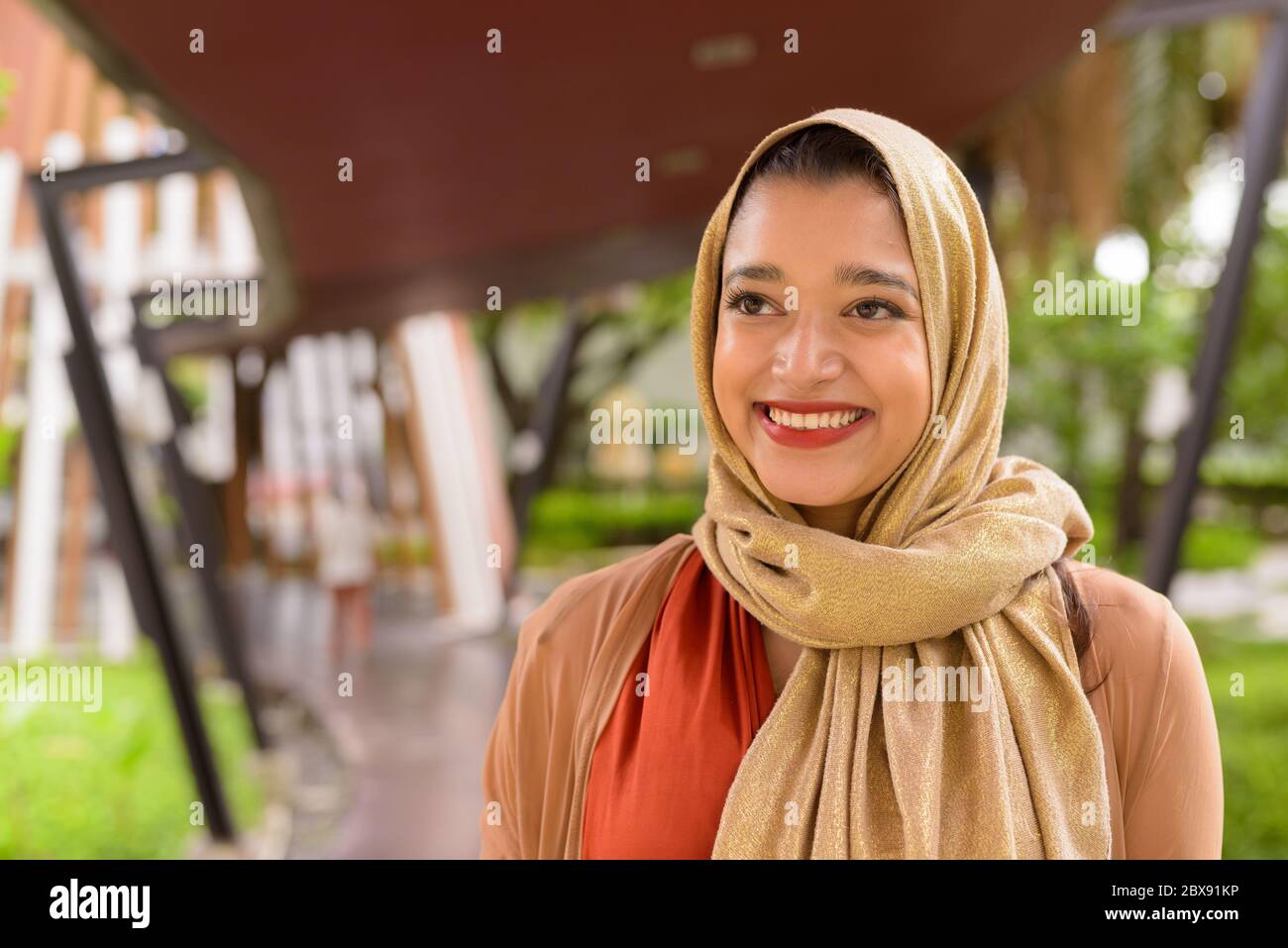 Face of happy young beautiful Indian Muslim woman thinking in the city ...