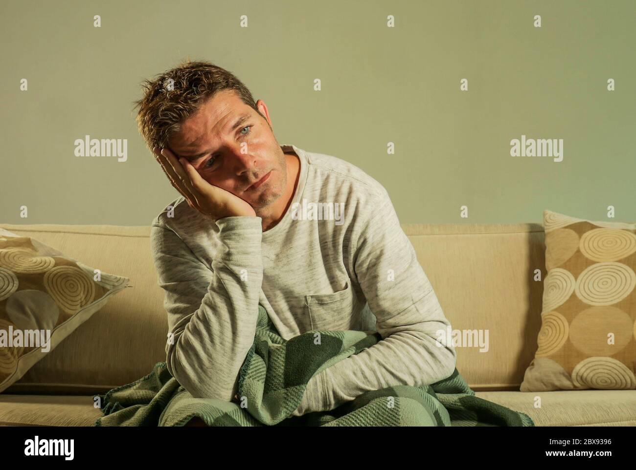 young sad and desperate man at home sitting at living sofa couch ...