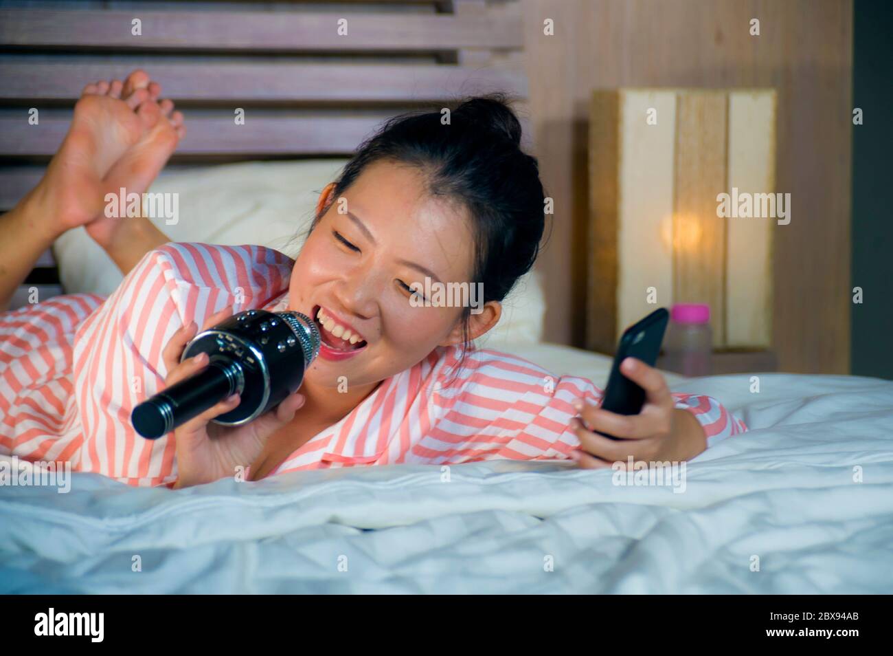 Young happy and beautiful Asian Japanese teenager girl singing karaoke ...