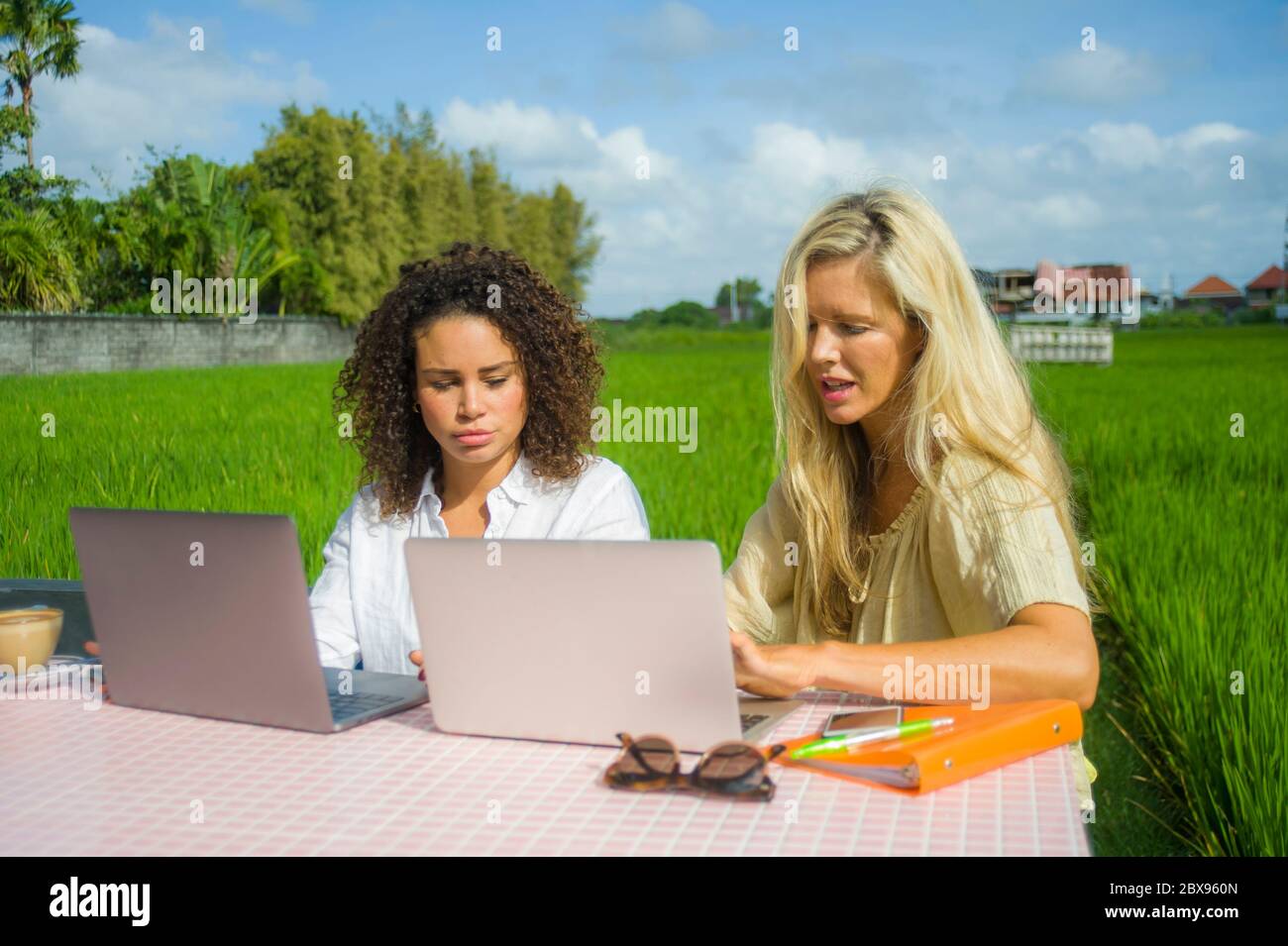 two happy female friends working outdoors at beautiful internet cafe ...