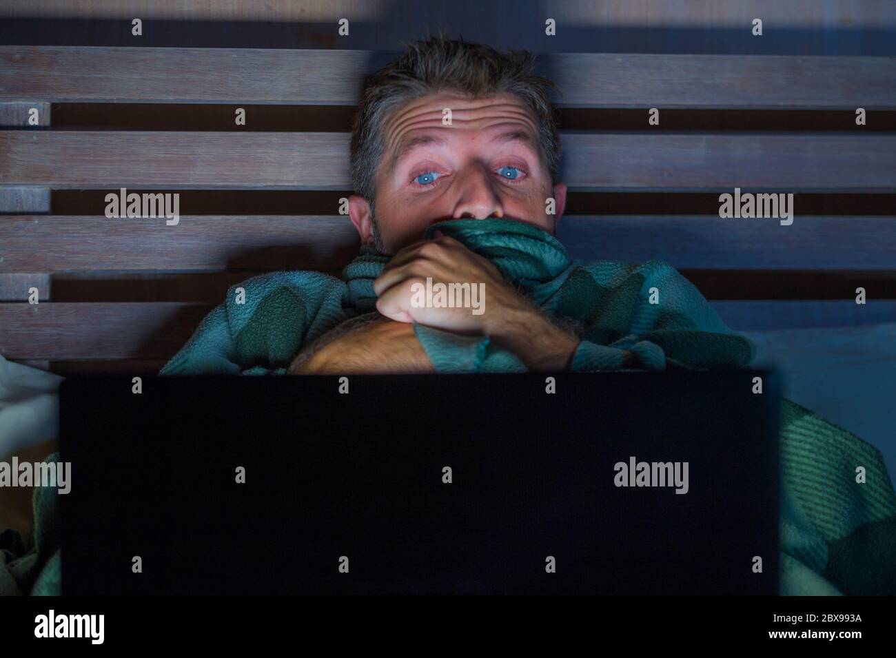 lifestyle portrait of young scared and stressed man in bed watching ...