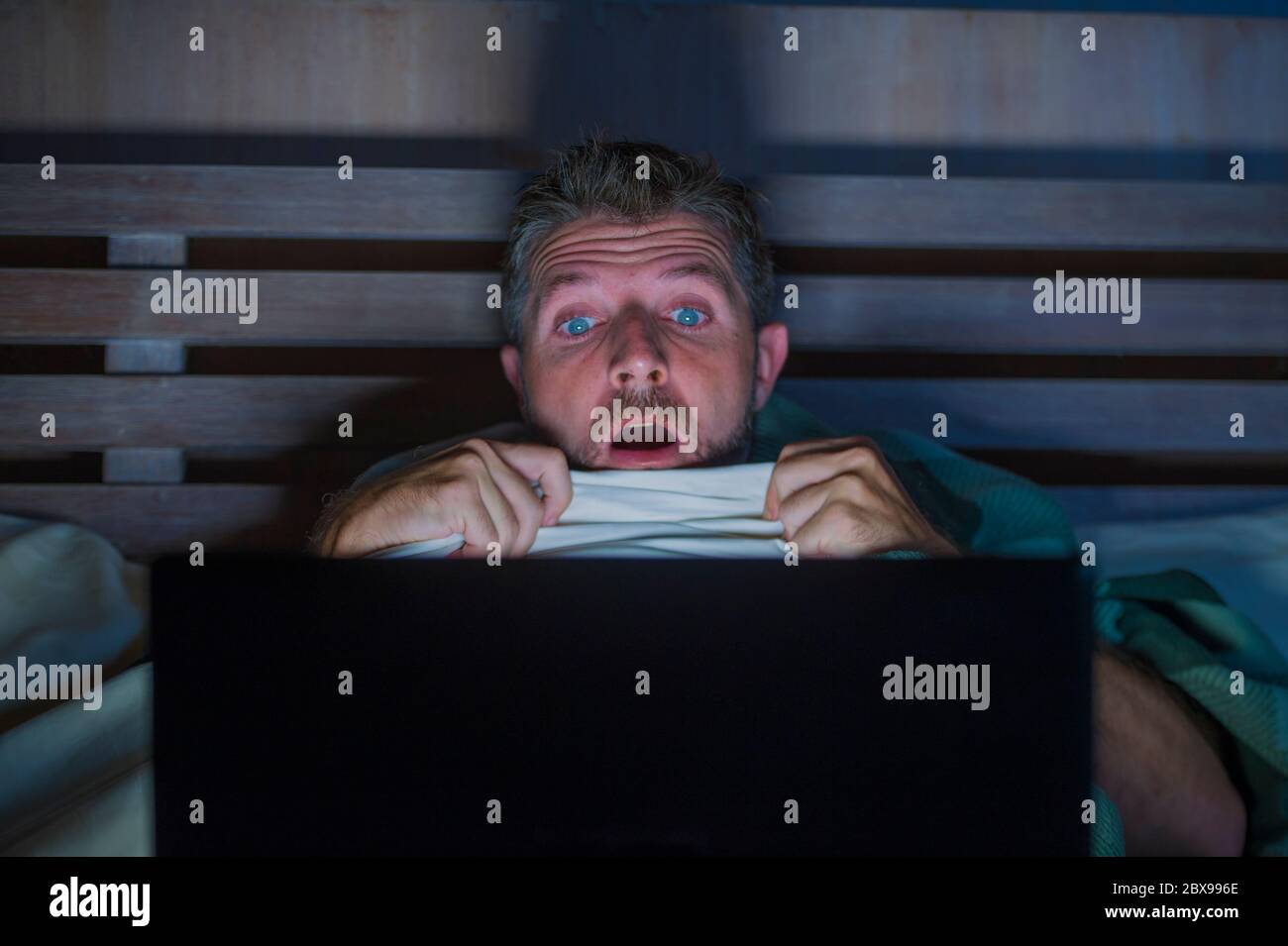 lifestyle portrait of young scared and stressed man in bed watching ...