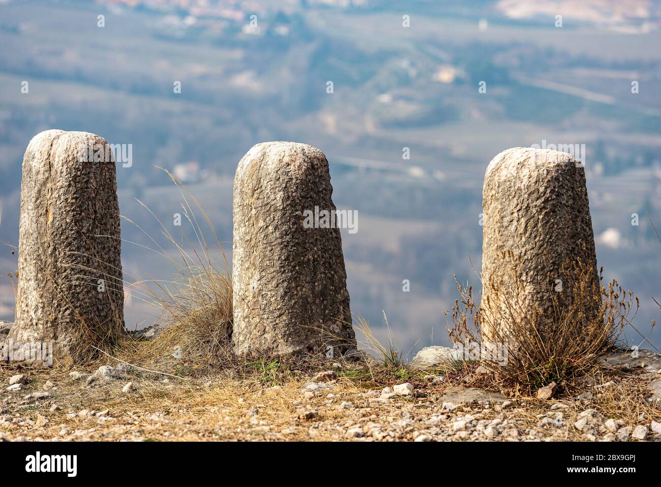 Three ancient stone bollards placed at the edge of a dirt road, used as ...