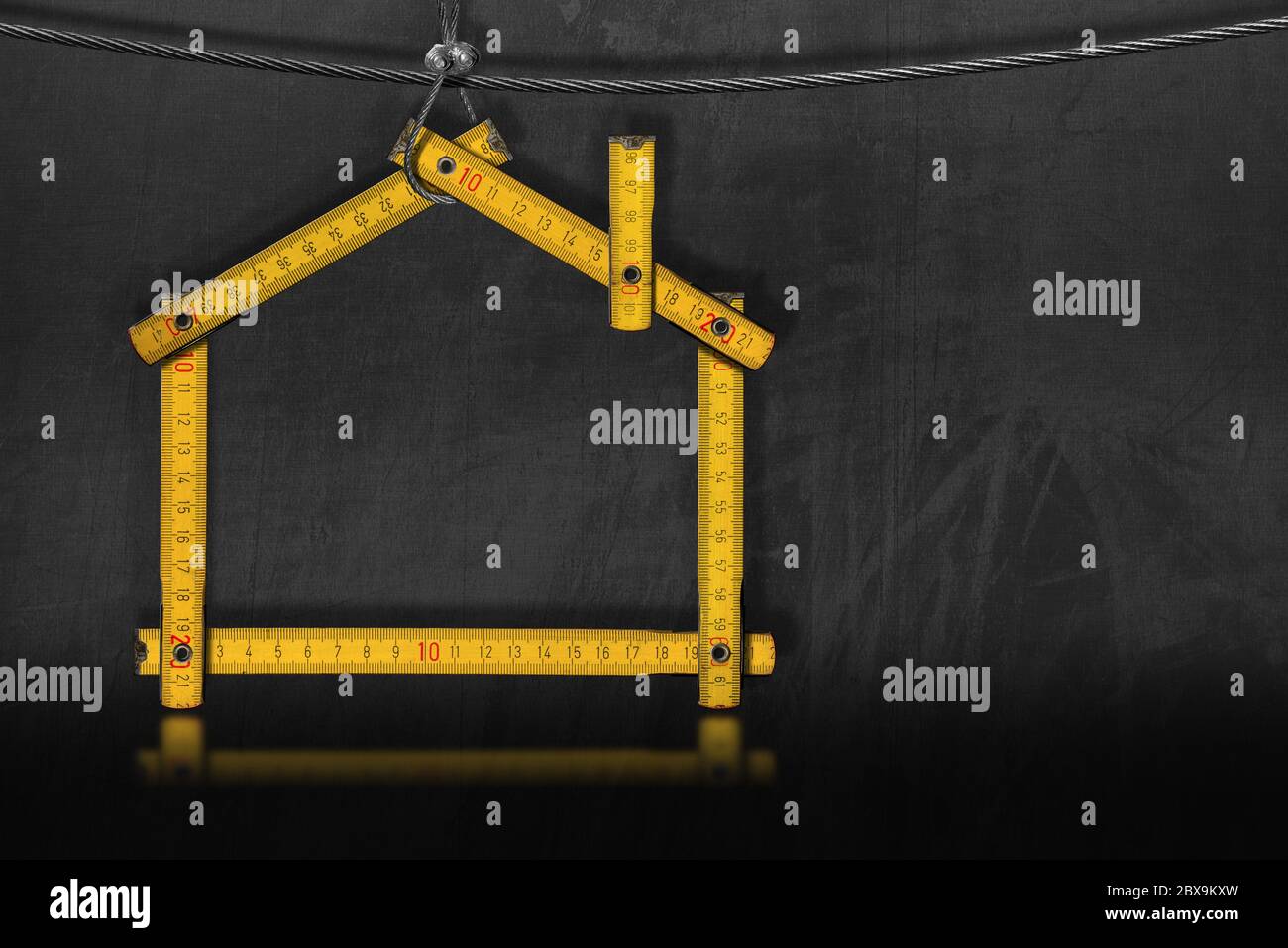 Yellow wooden folding ruler in the shape of a house hanging on a steel ...