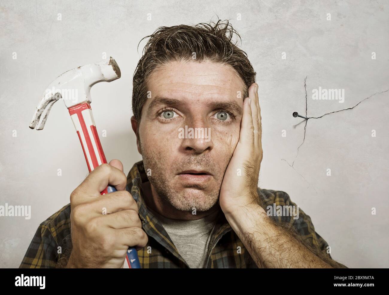 funny portrait of man holding hammer after driving a nail for hanging a ...