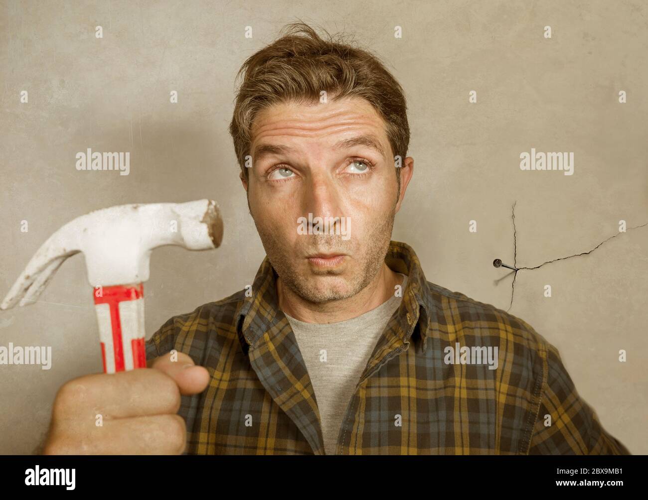 funny portrait of man holding hammer after driving a nail for hanging a ...