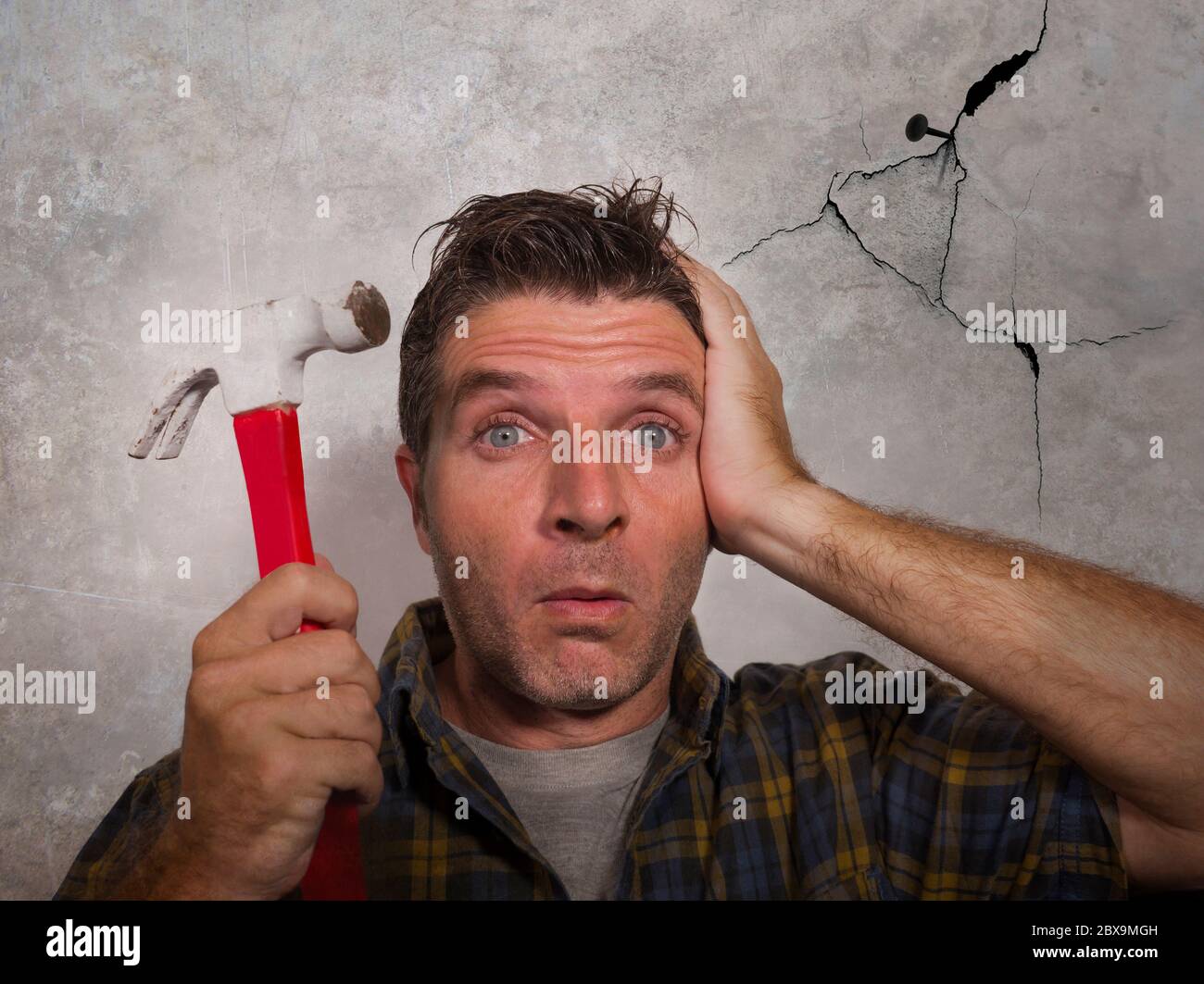 funny portrait of man holding hammer driving a nail for hanging a frame ...