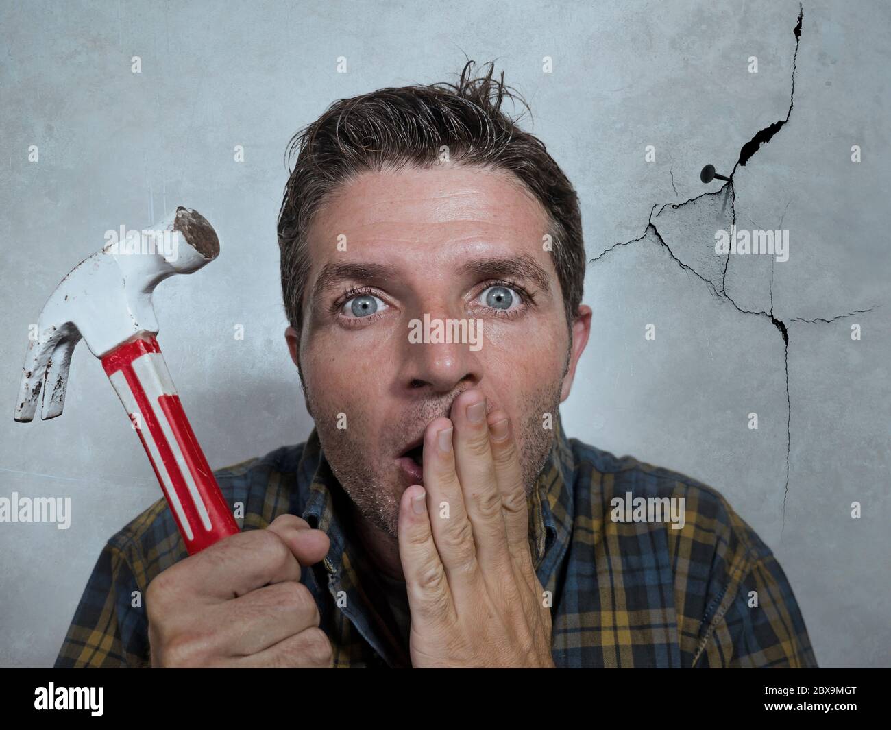 funny portrait of man holding hammer driving a nail for hanging a frame ...