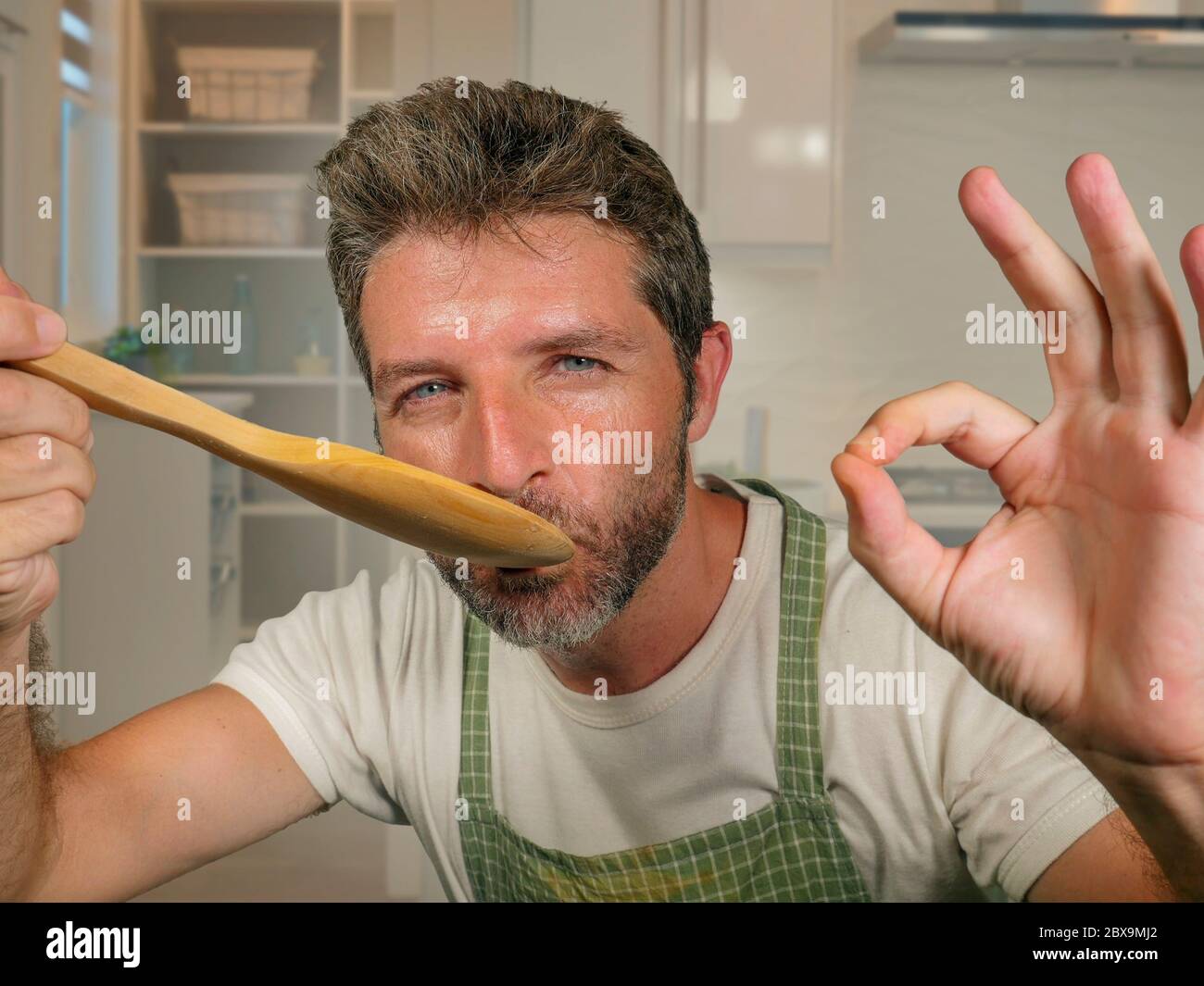 lifestyle portrait of young happy and attractive home cook man in apron ...