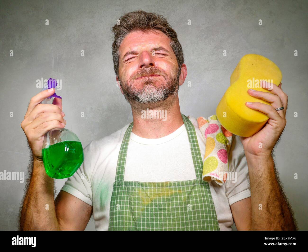 isolated portrait of 30s man in apron holding sponge and detergent ...