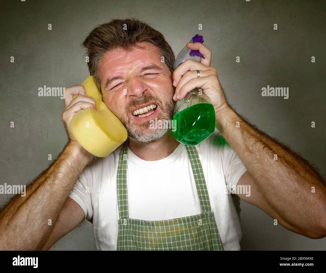 isolated portrait of 30s man in apron holding sponge and detergent ...