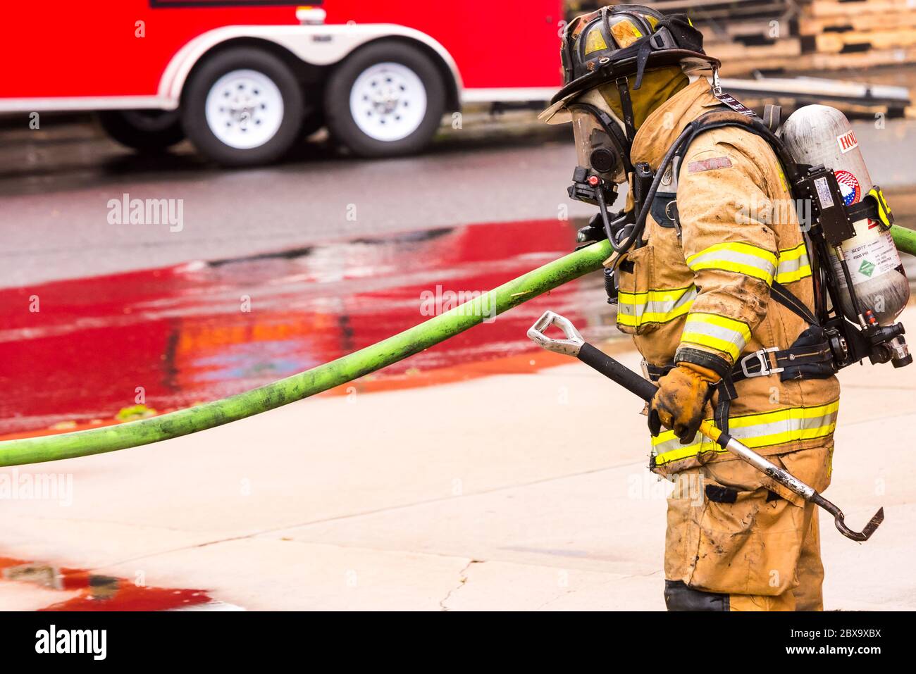 Firefighter wearing uniform and oxygen tank, carrying a large tool ...