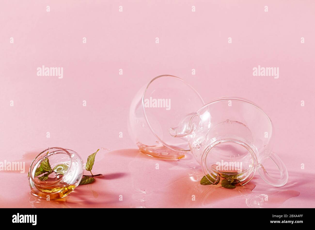 thrown glass teapot and spilled tea on a pink background. abstract ...