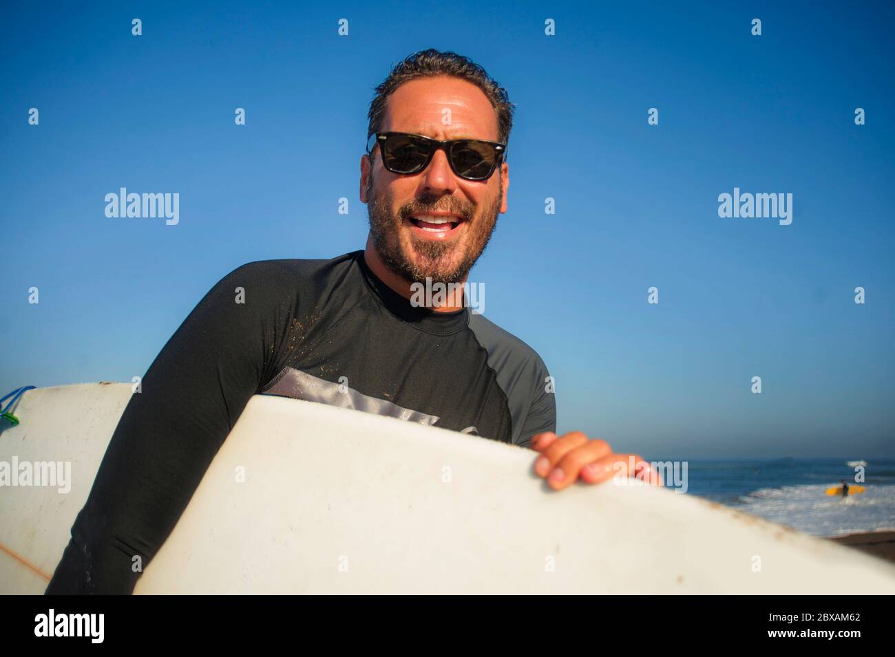 lifestyle beach portrait of handsome and attractive surfer man in ...