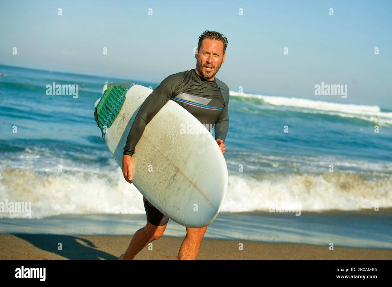 lifestyle beach portrait of handsome and attractive surfer man in ...