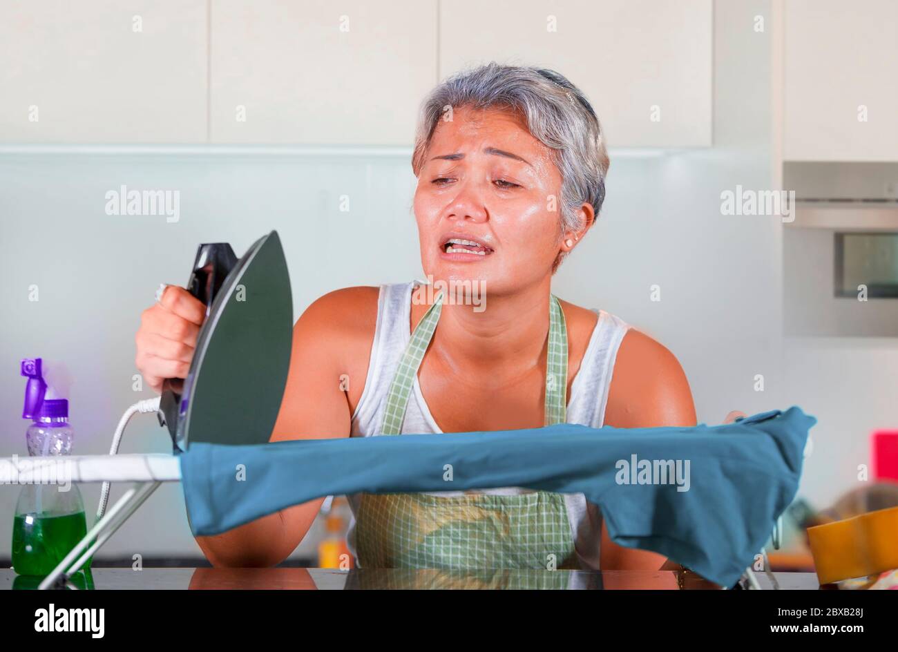 desperate and stressed middle aged Asian woman ironing in stress at ...