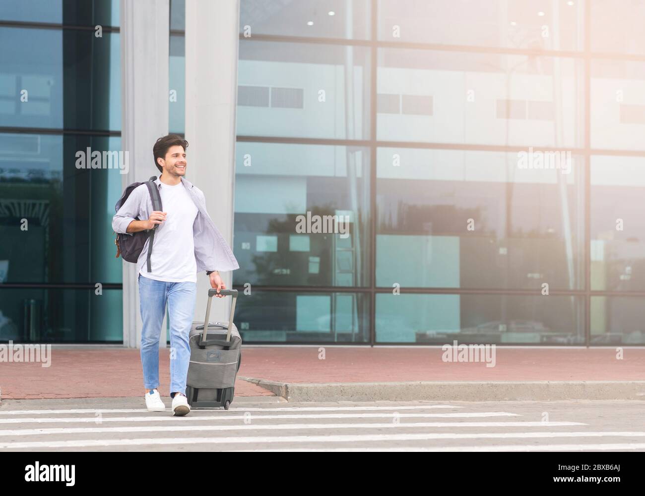 Handsome young man walking with luggage out of airport, carrying ...