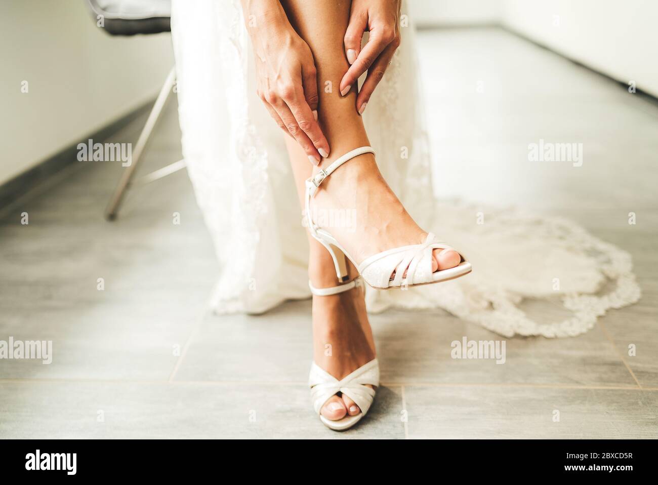 Bride putting on white shoes on her tender feet. Woman in wedding gown ...