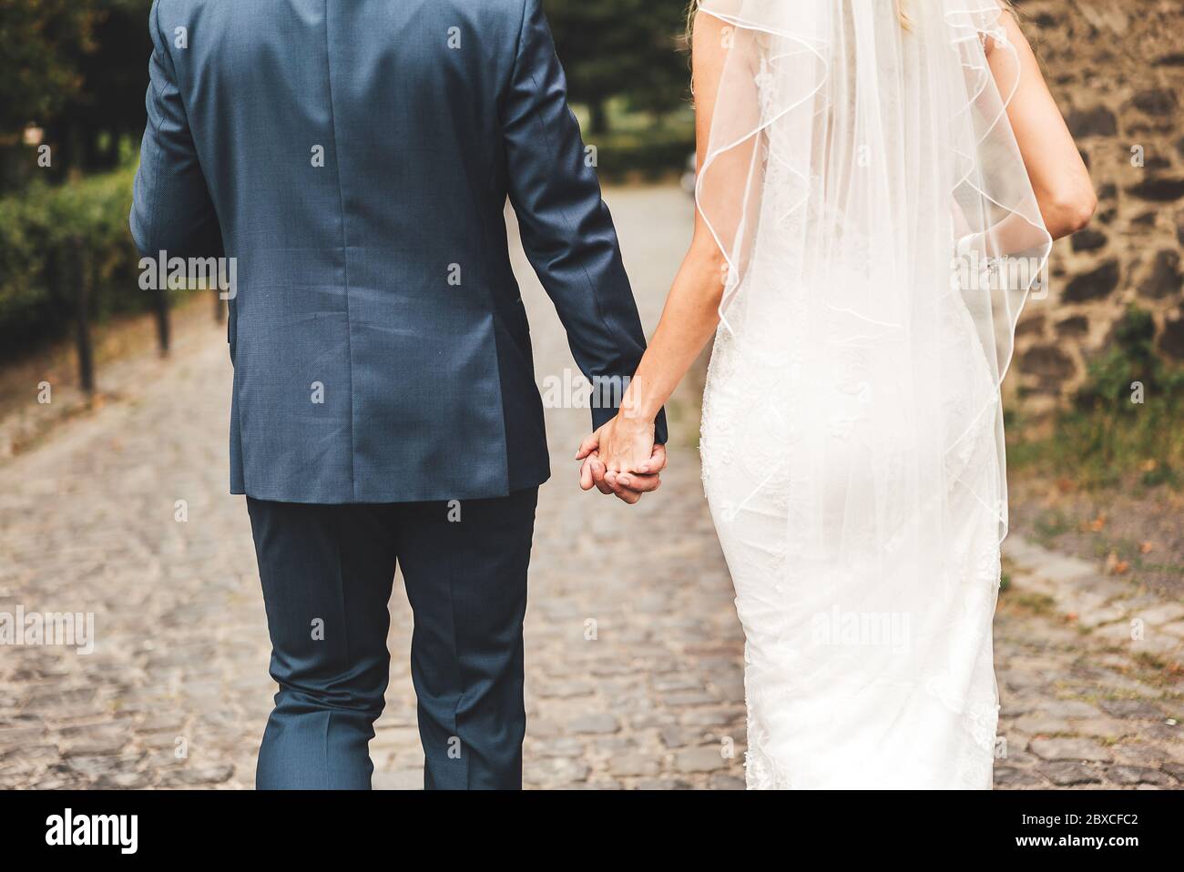 Rear view of married couple walking on stone-paved road. Groom and ...