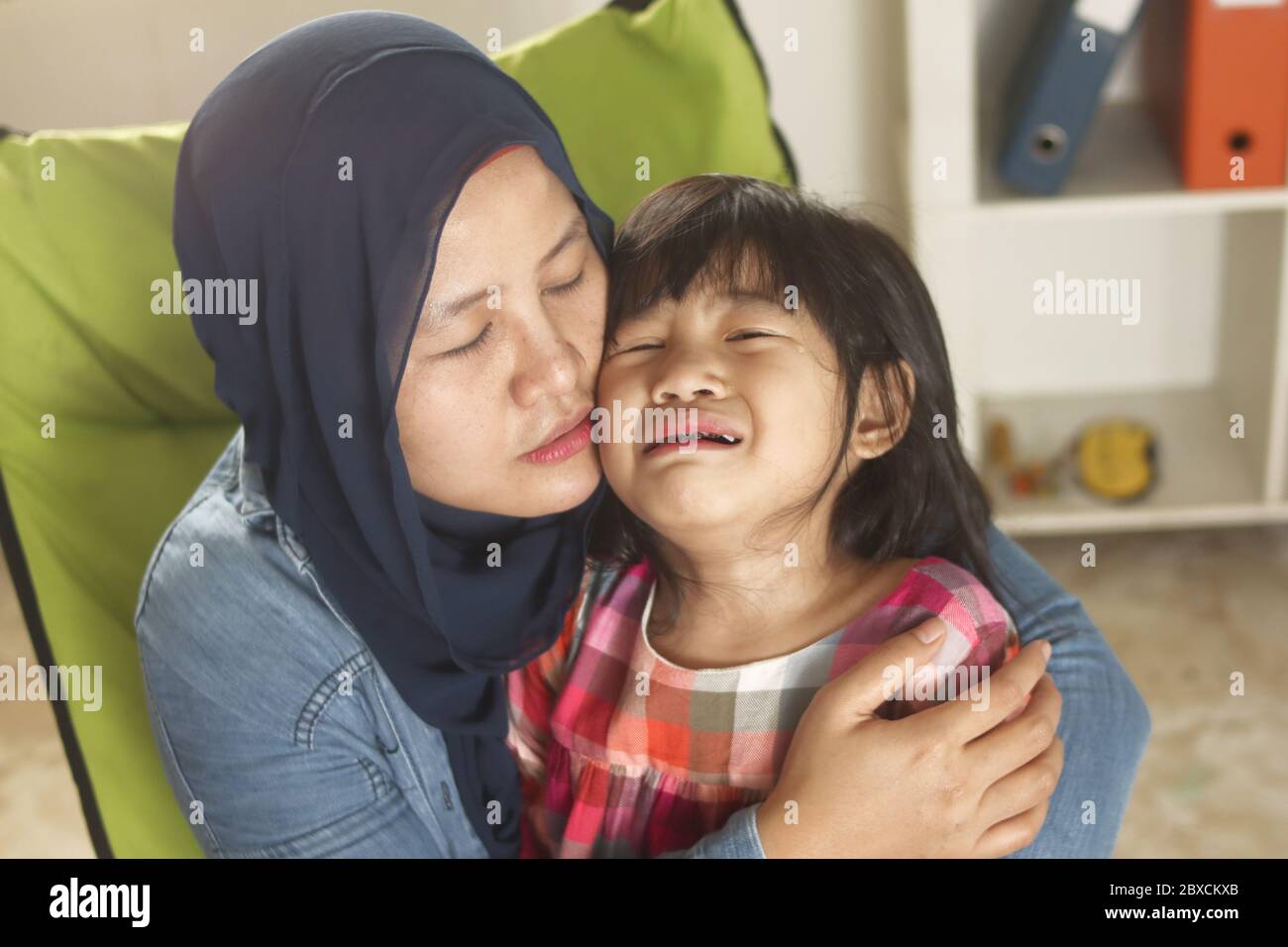 Asian muslim mother wearing hijab calming her sad and crying daughter ...