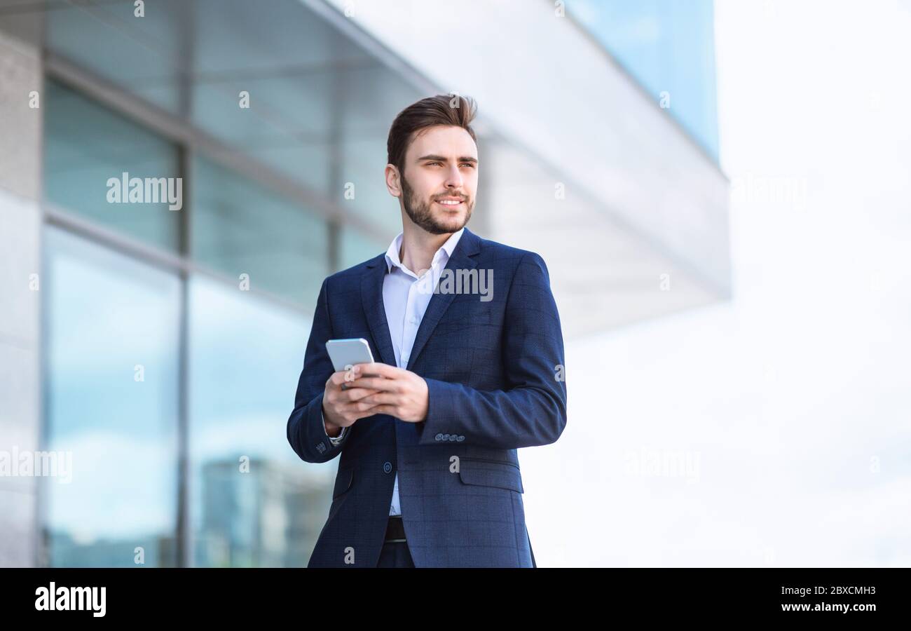 Handsome financier in business suit browsing web on his smartphone ...