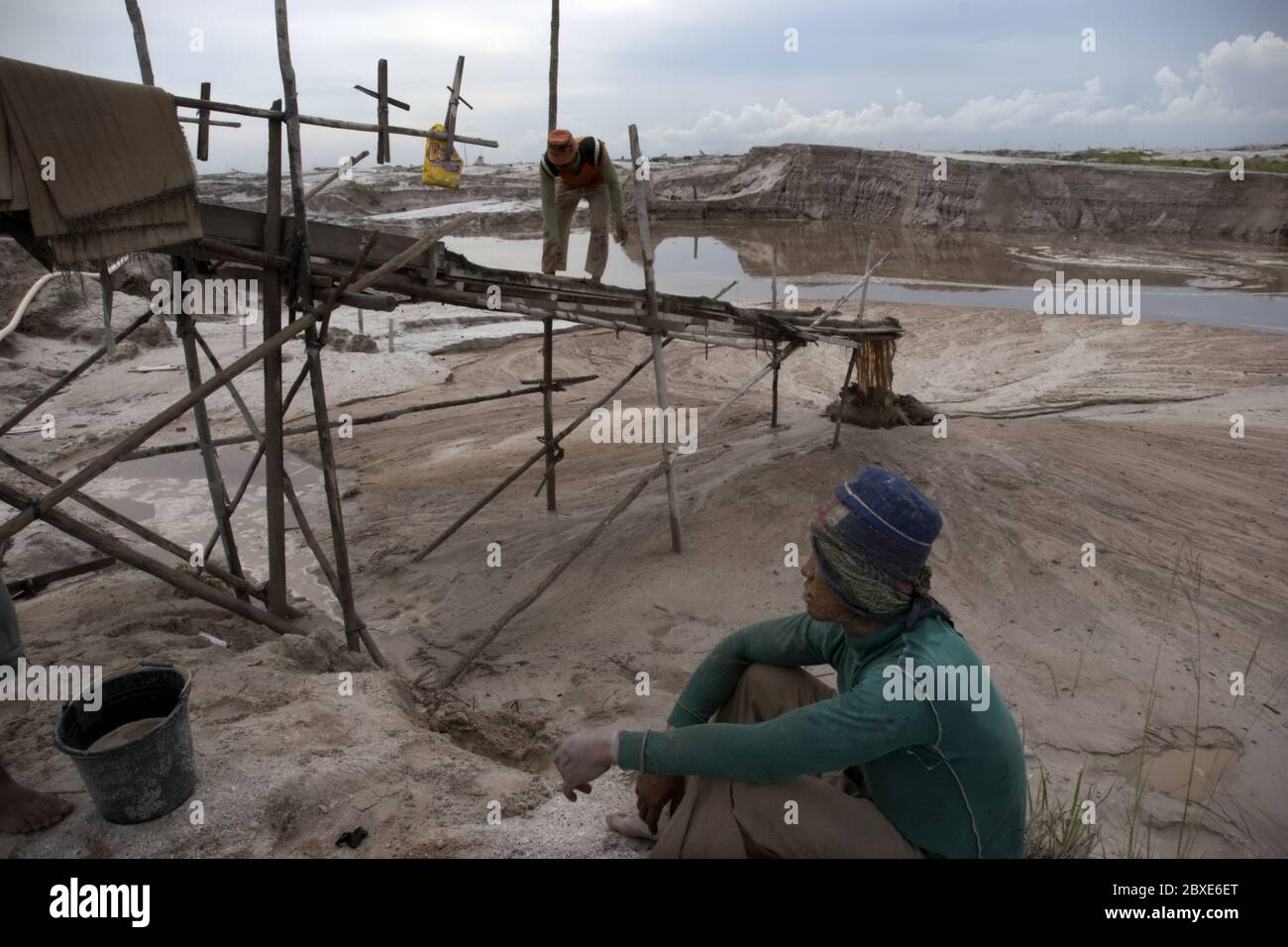 A worker sitting on the ground, while a co-worker checking the sluice ...
