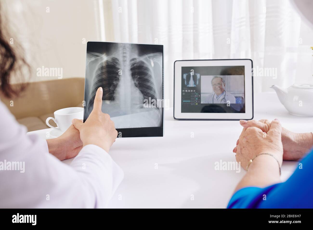 Pulmonologist checking lungs x-ray of senior woman and video calling ...