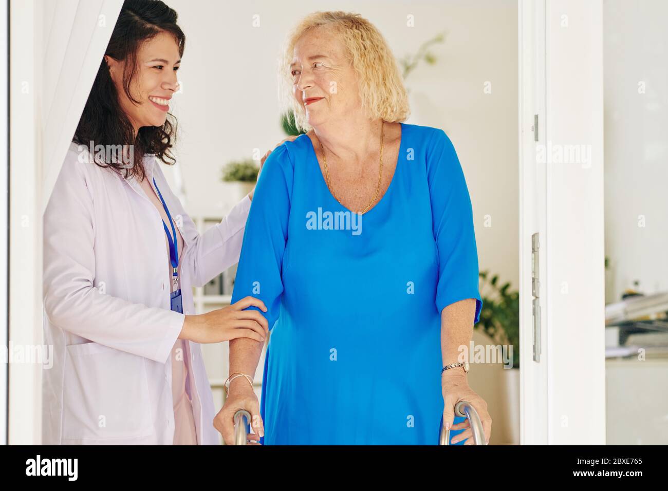 Smiling pretty medical nurse helping her senior patient to use front ...