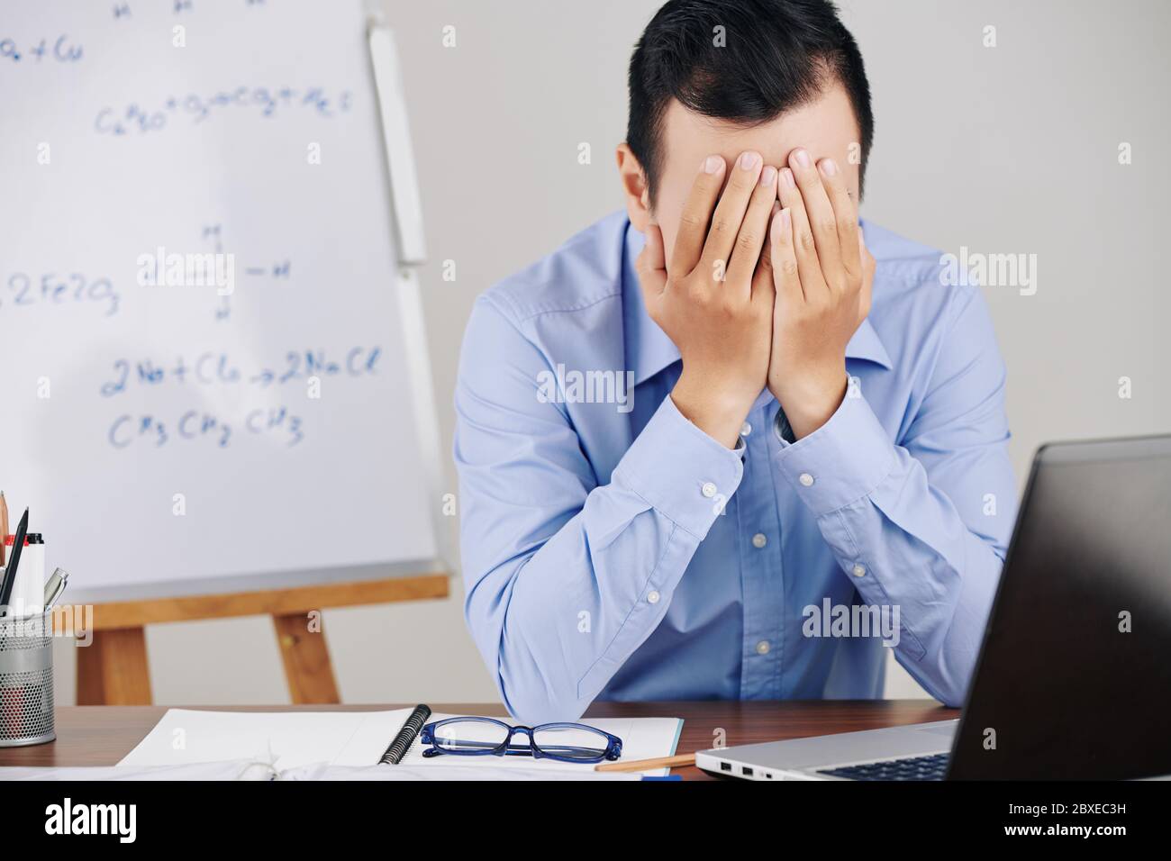 Stressed and tired teacher covering his face after conducting online ...