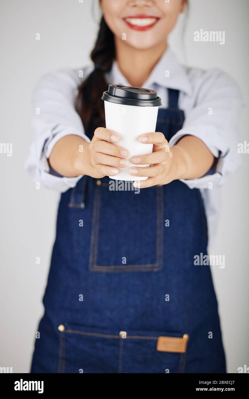 Close-up image of young female barista in denim apron giving cup of ...