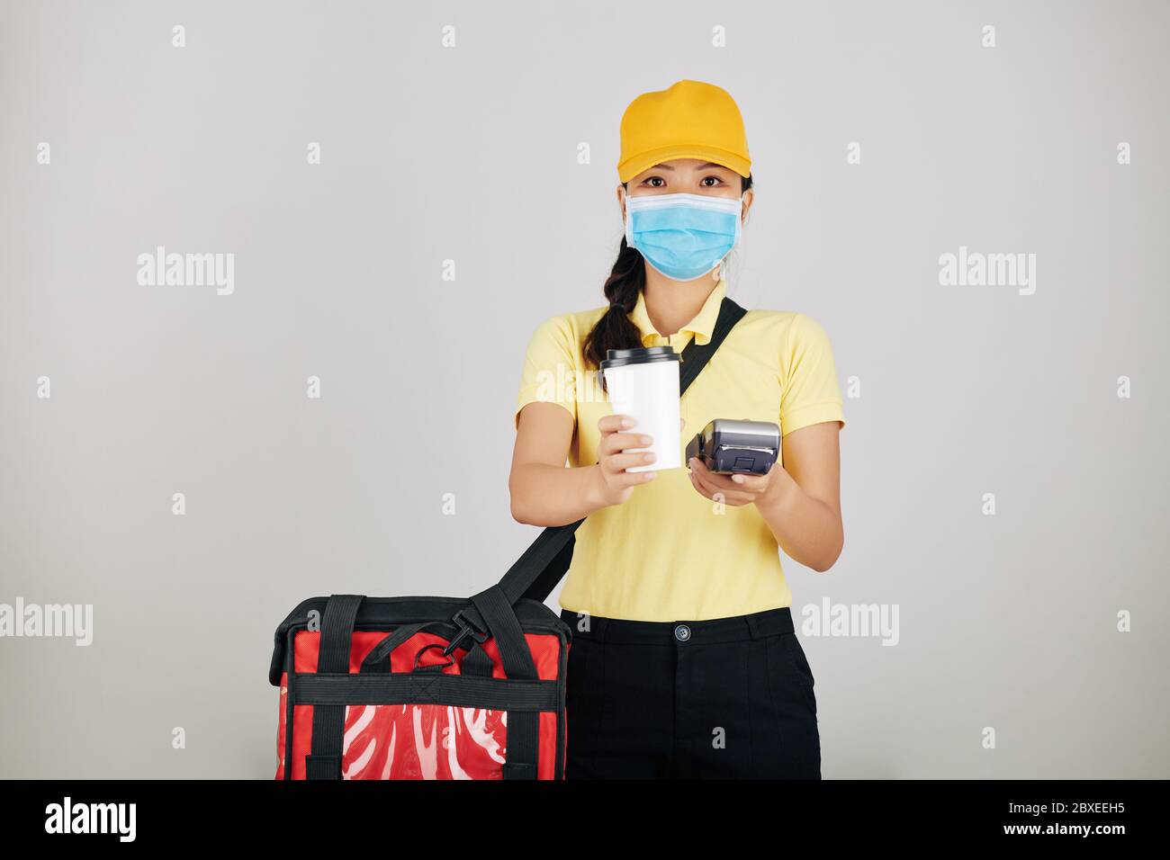 Pretty young Asian delivery service worker giving cup of coffee and ...