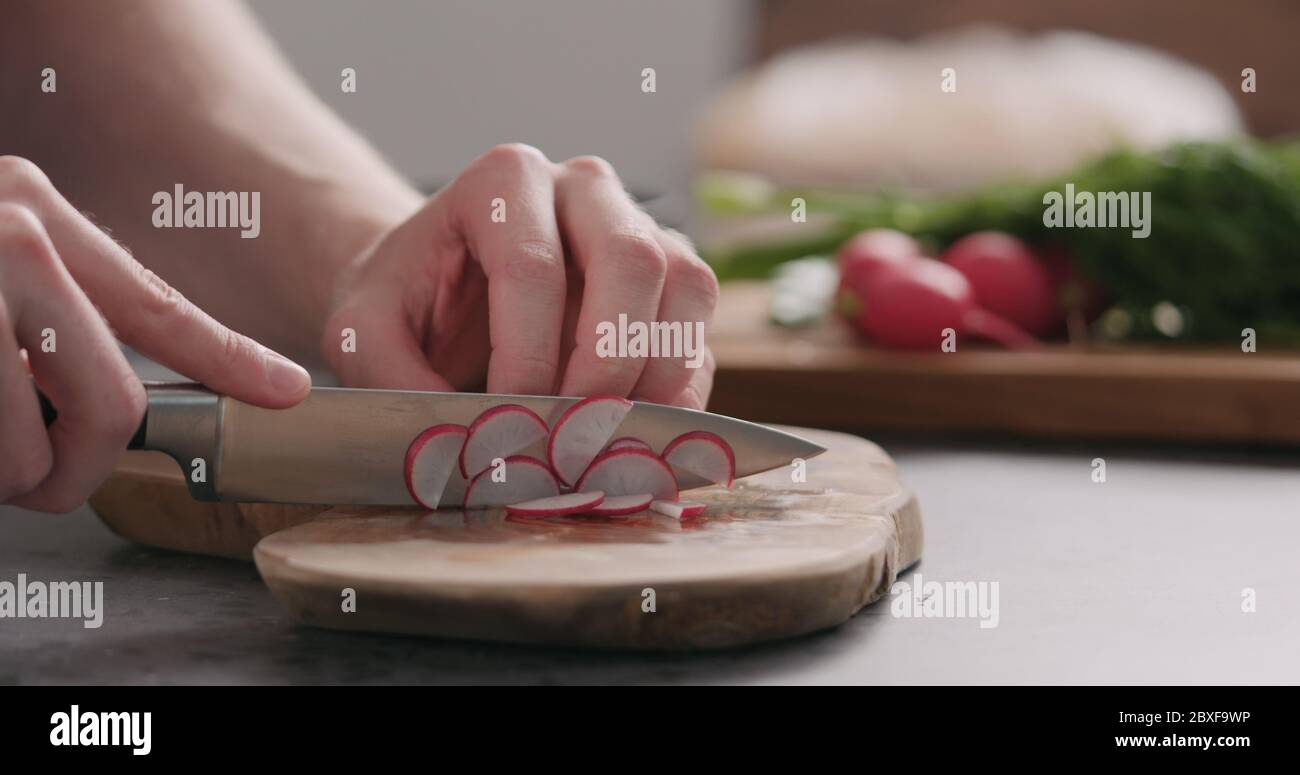 man slicing fresh radish on olive board side view Stock Photo - Alamy