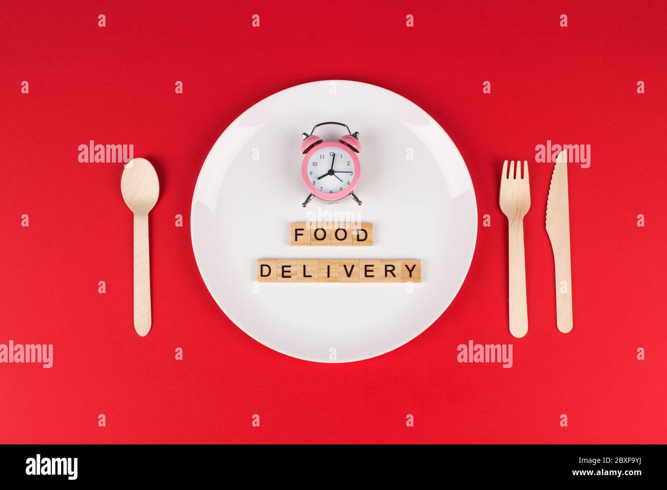 White plate, pink alarm clock, wooden cutlery set and words FOOD ...
