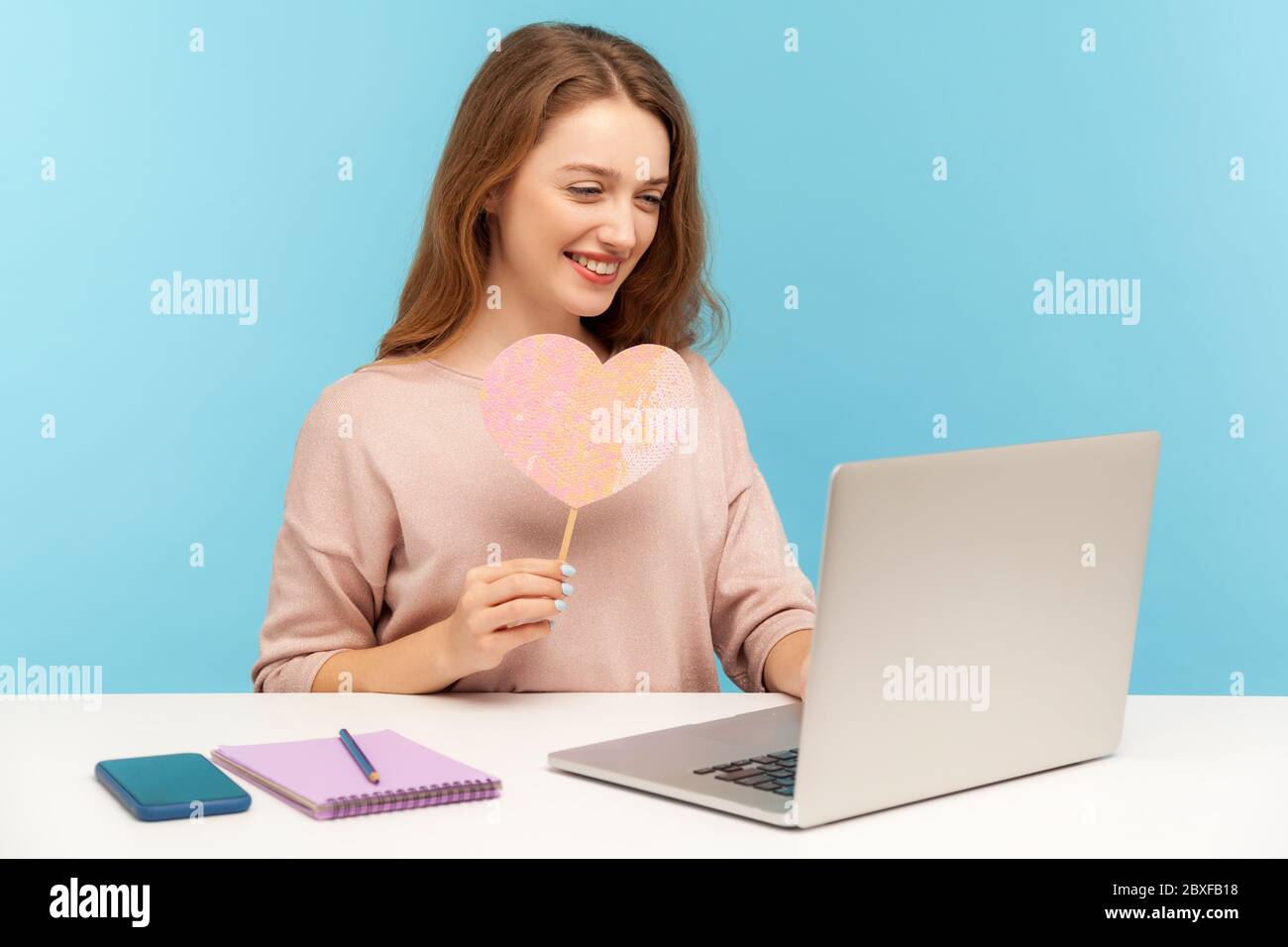Lovely feminine woman holding pink heart and talking on video call on ...