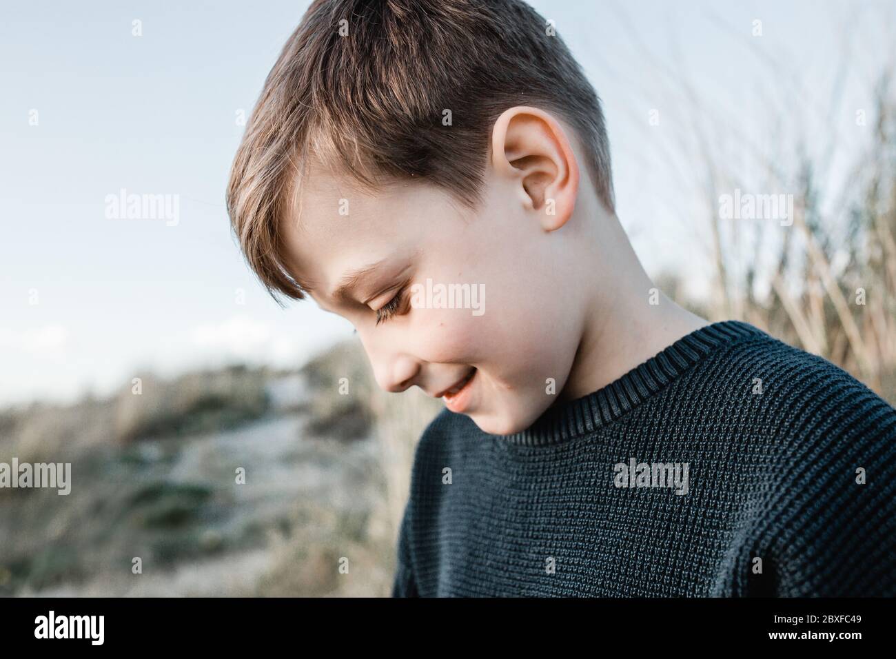 autistic boy sitting in sand dunes looking down shy Stock Photo - Alamy