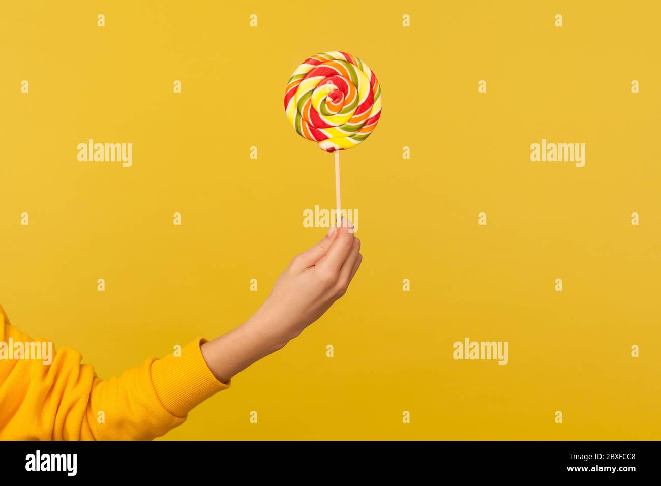 Closeup of hand holding appetizing round rainbow candy on stick, big ...