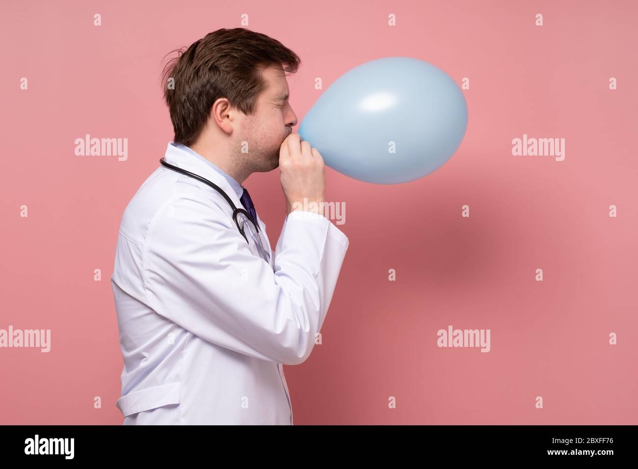 Young caucasian man blowing a blue balloon on colored background ...